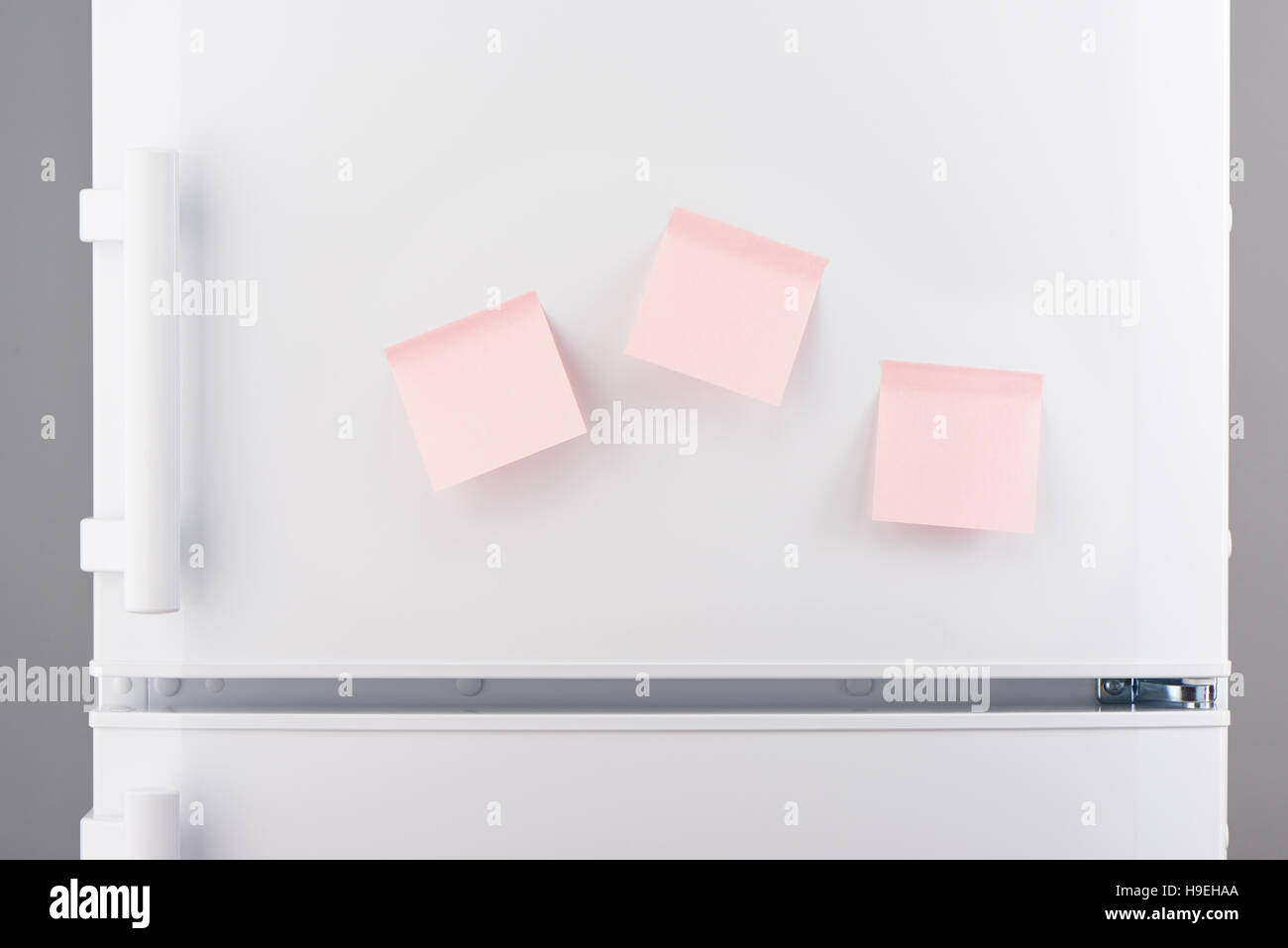 Three blank light pink sticky paper notes on white refrigerator door ...