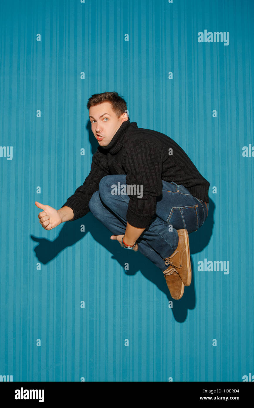 Portrait of young man with serious facial expression jumping over blue ...
