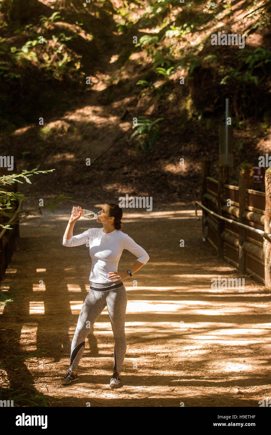 Woman drinking water on sunny forest path Stock Photo - Alamy