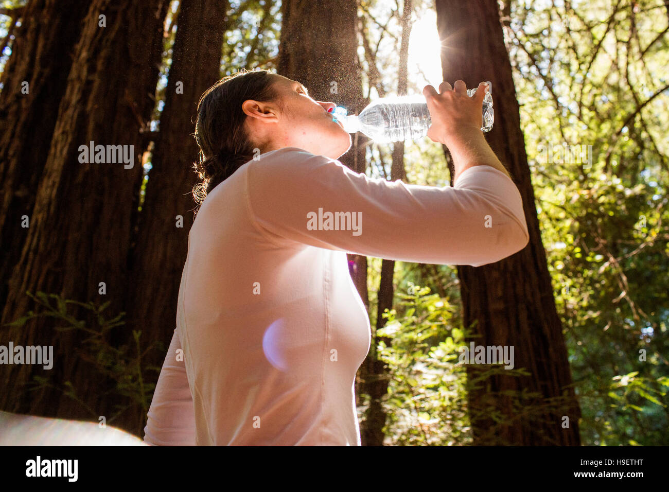 Woman drinking water from bottle in sunny forest Stock Photo - Alamy
