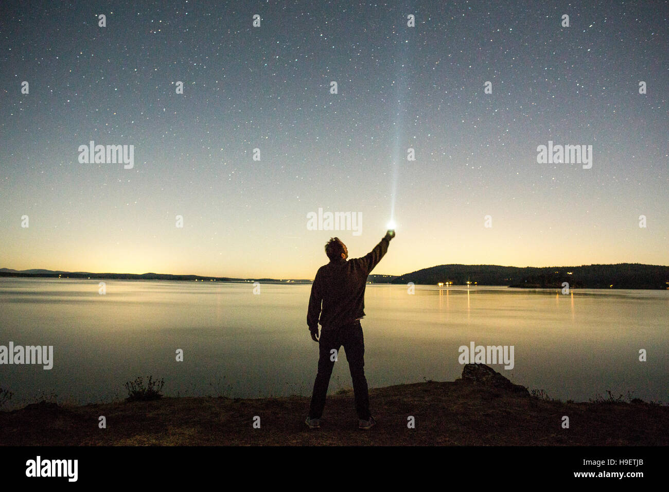 Caucasian man pointing flashlight at night sky near water Stock Photo ...