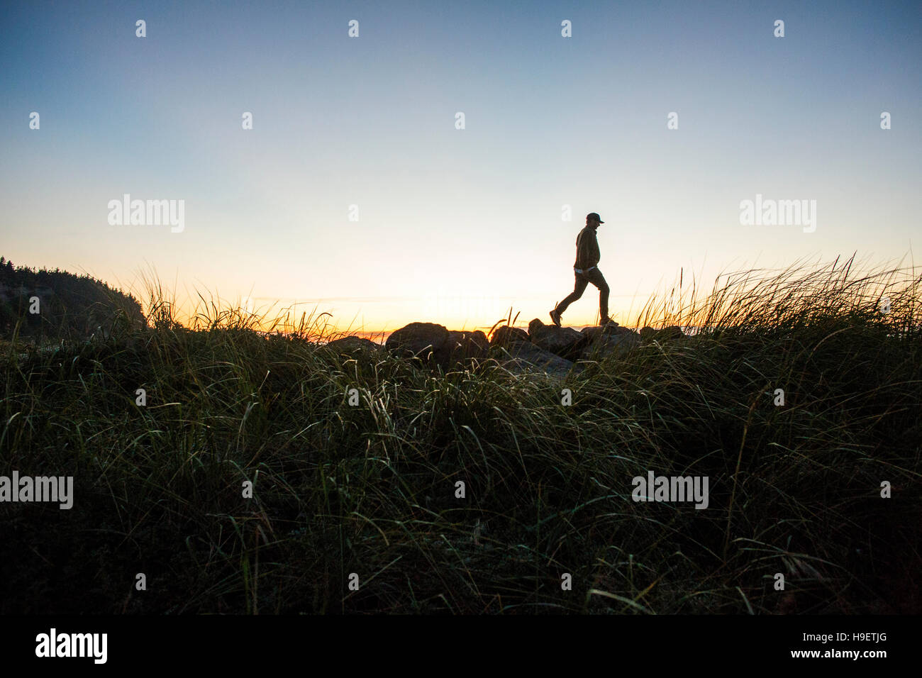 Silhouette Of Distant Caucasian Man Walking On Rocks At Sunset Stock