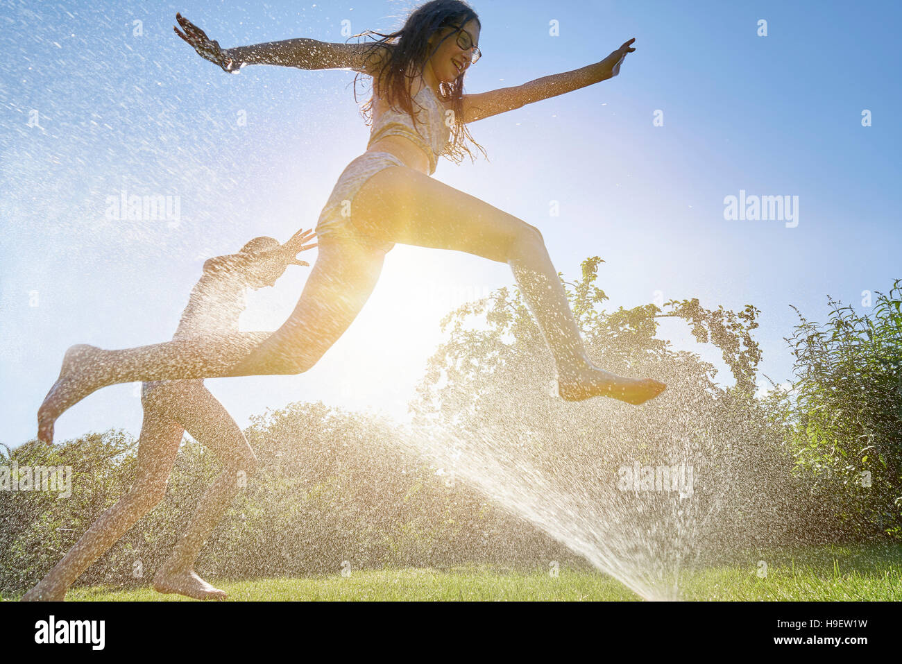 Girl jumping through sprinkler hi-res stock photography and images - Alamy