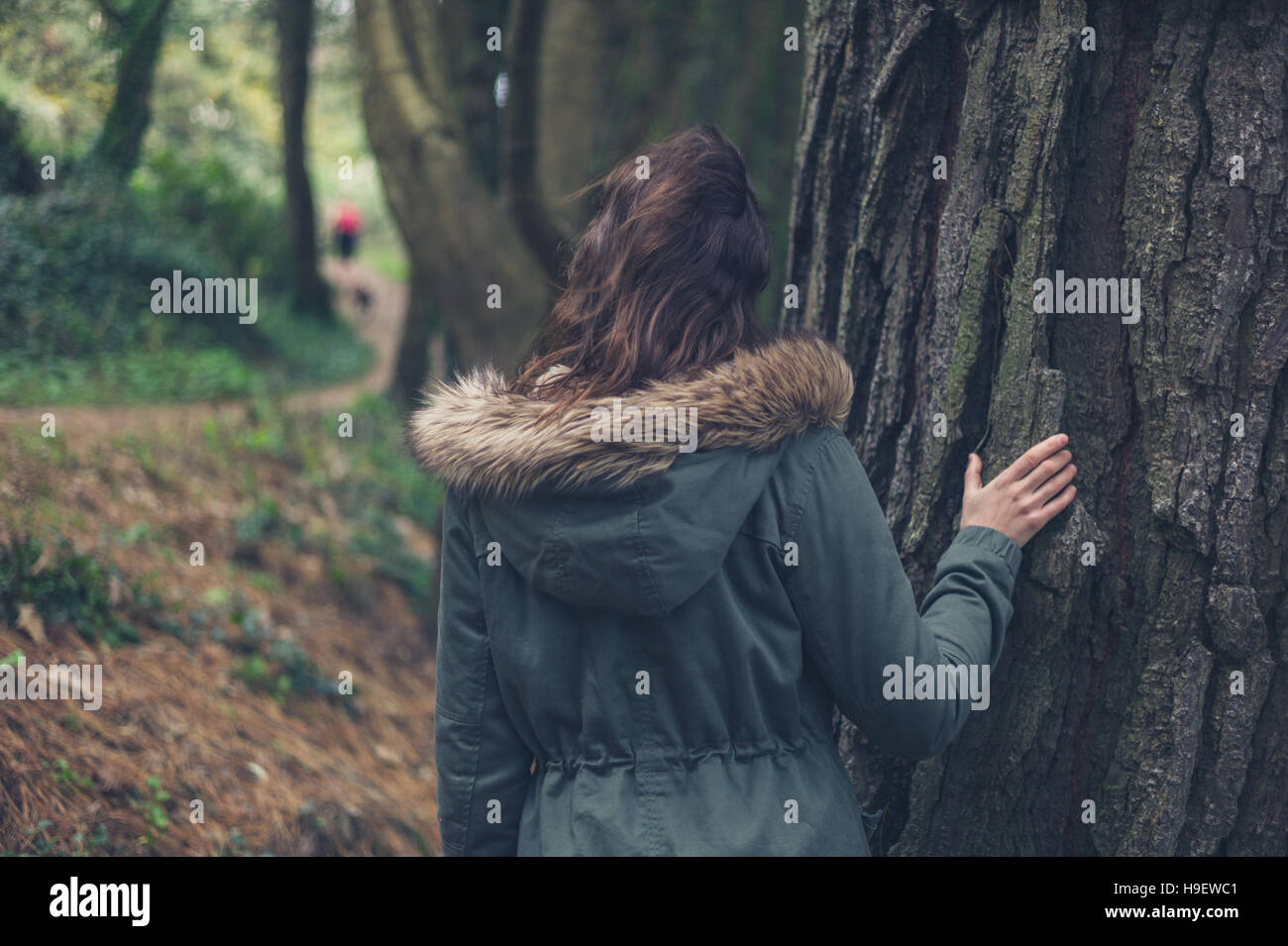 A young woman wearing a winter coat is standing by a big tree in the ...