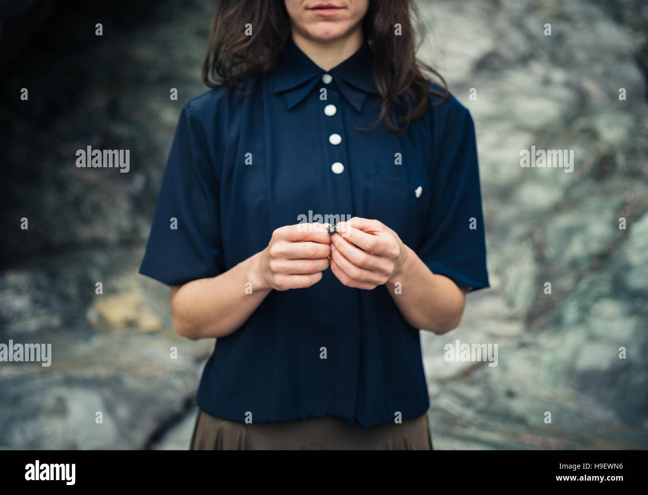 A young woman is standing outside in nature by a rock and is holding a ...
