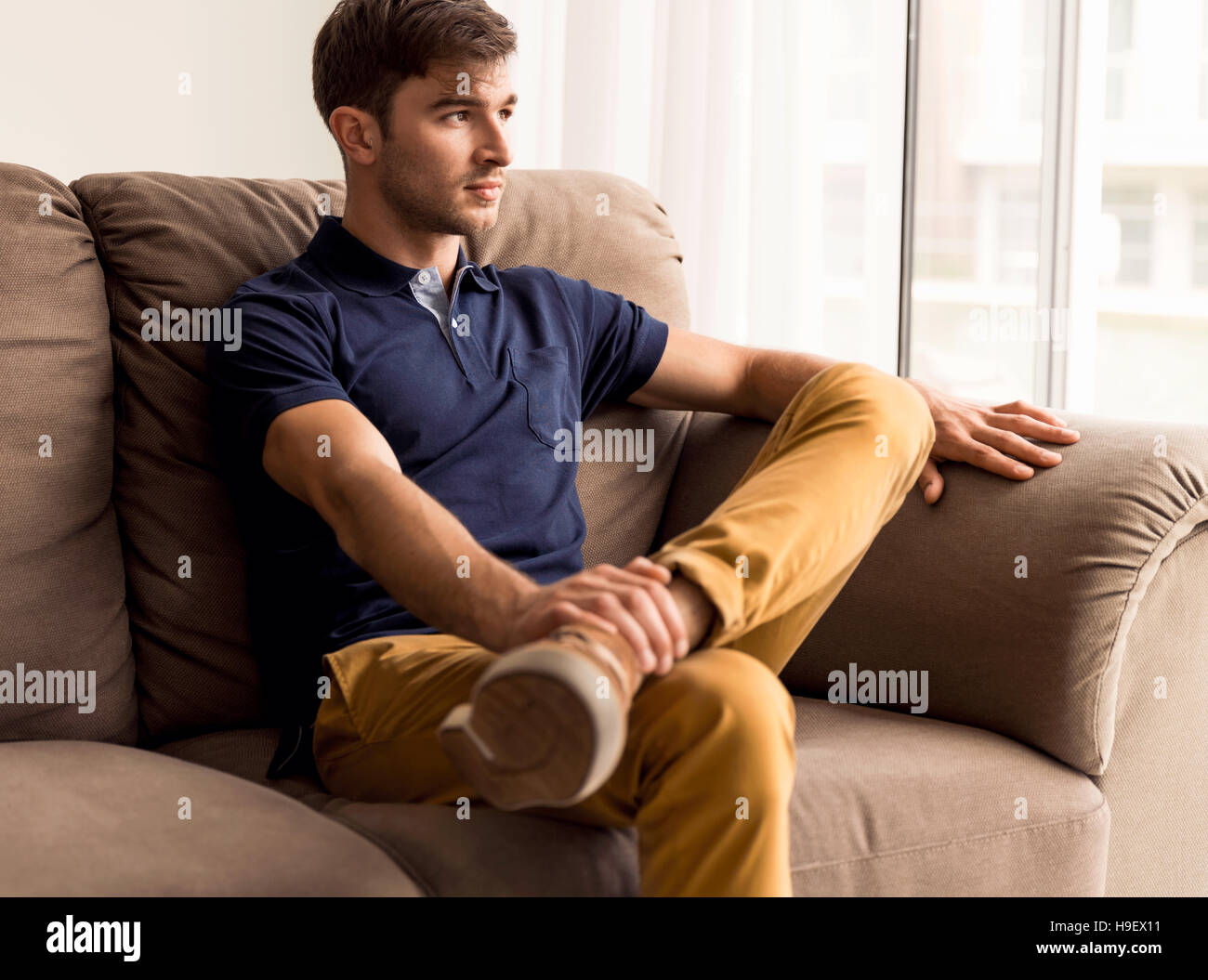Portrait of a handsome young man sitting on the sofa Stock Photo - Alamy