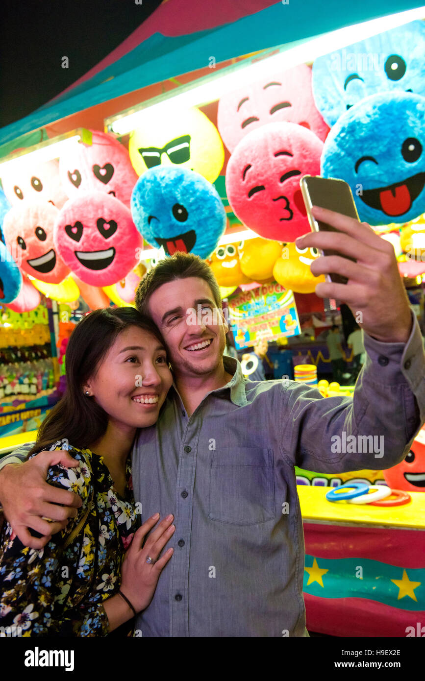 Smiling couple posing for cell phone selfie in amusement park Stock ...
