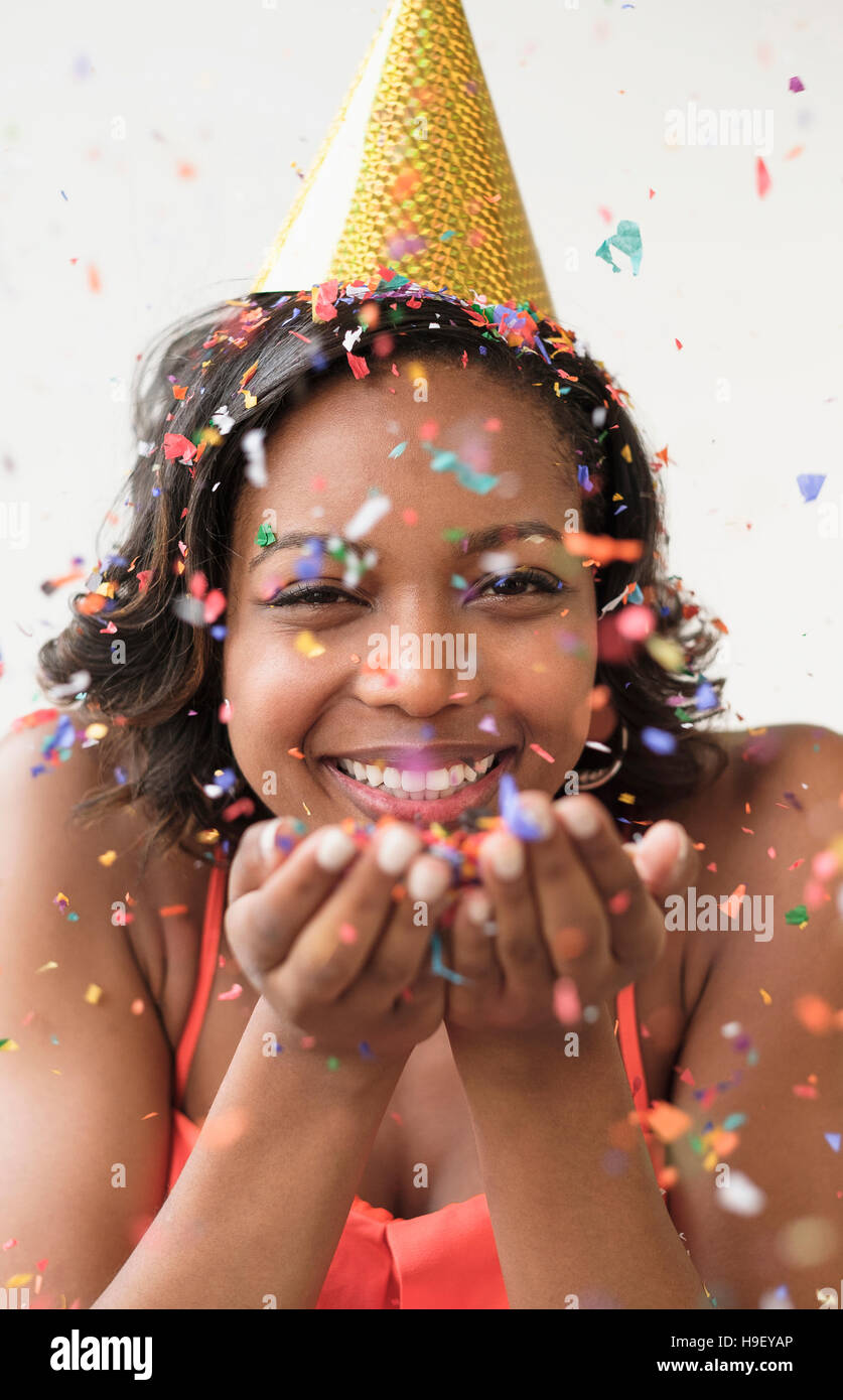 Mixed Race woman wearing party hat blowing confetti Stock Photo - Alamy
