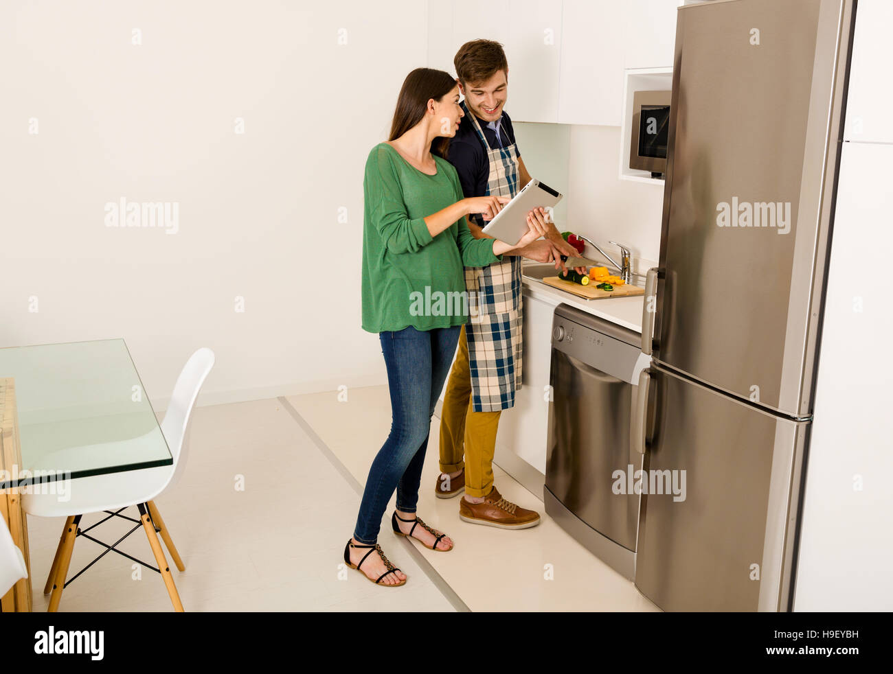 Young couple on the kitchen follow a recipe by tablet and cooking Stock ...