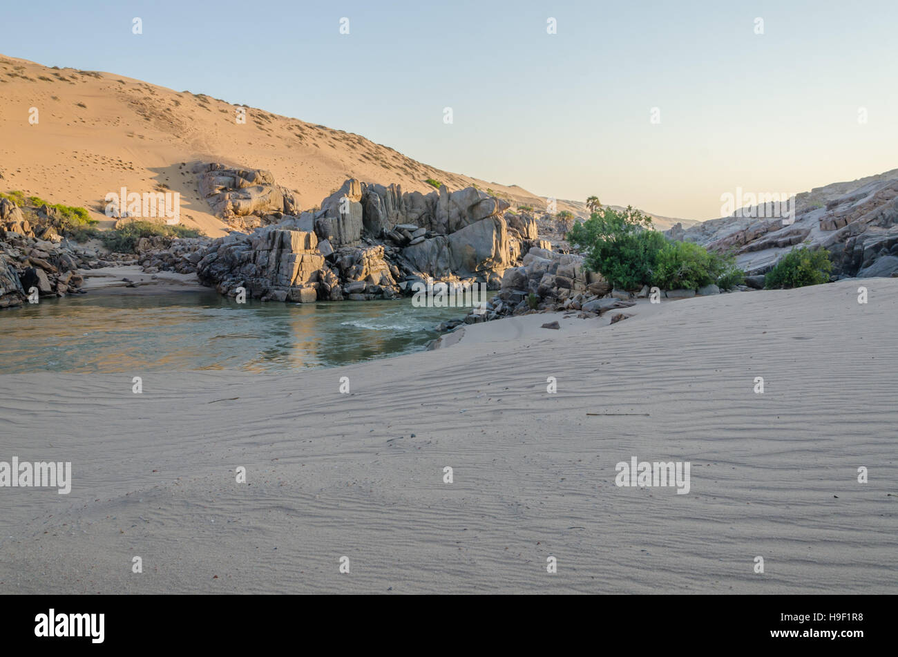 Kunene River in front of towering ancient Namib Desert sand dunes of ...
