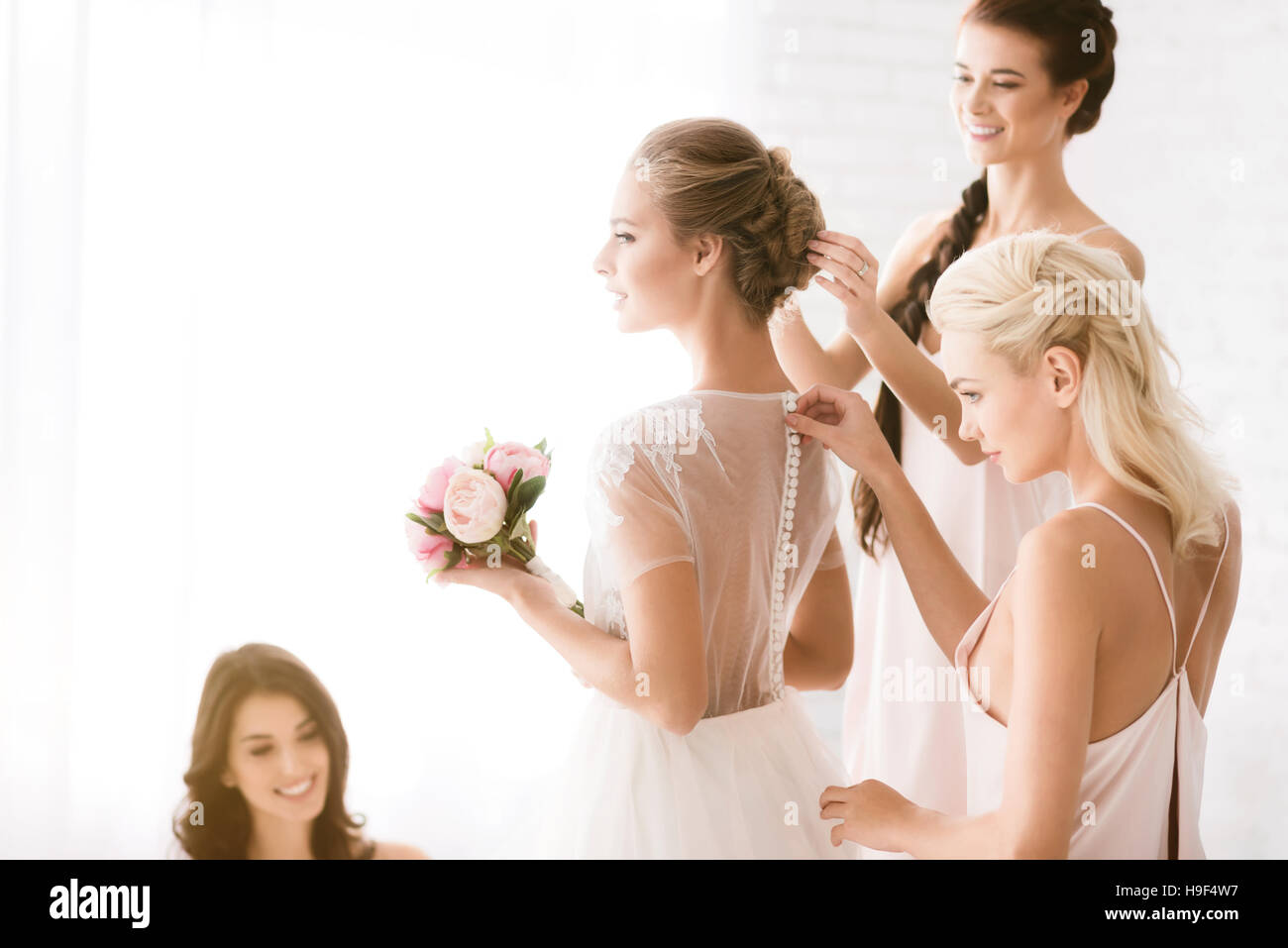 Delighted bridesmaids helping the bride to get ready Stock Photo - Alamy
