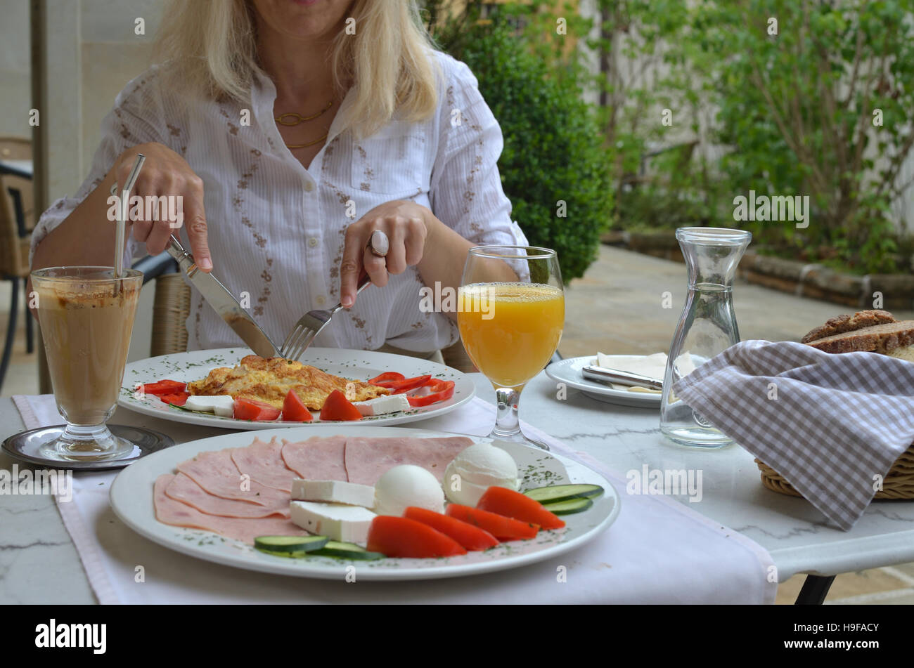 Blonde woman having colorful American breakfast at a table served for ...