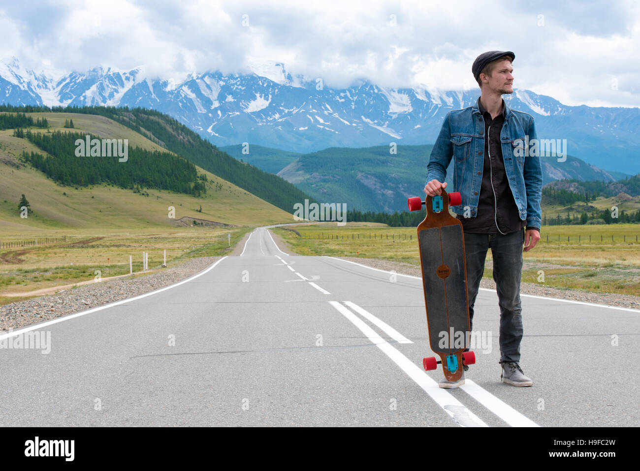 Longboarder posing beside his longboard skateboard on the mountain road ...