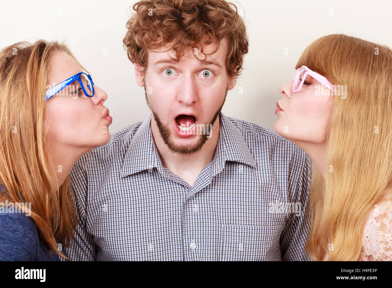 Two pretty young women in glasses kissing handsome man. Love triangle ...