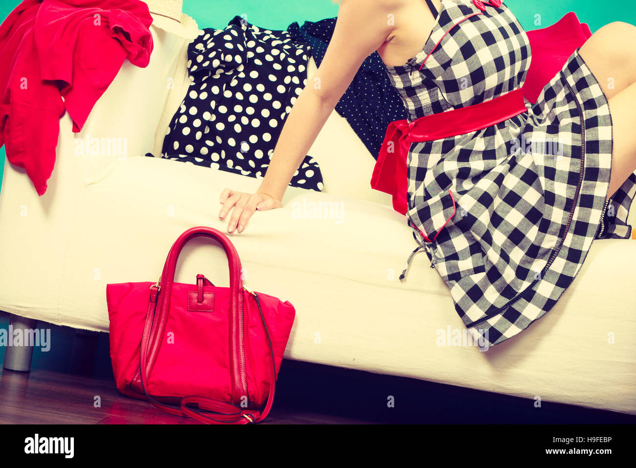 Woman wearing checked dress relaxing on sofa after shopping, red bag ...