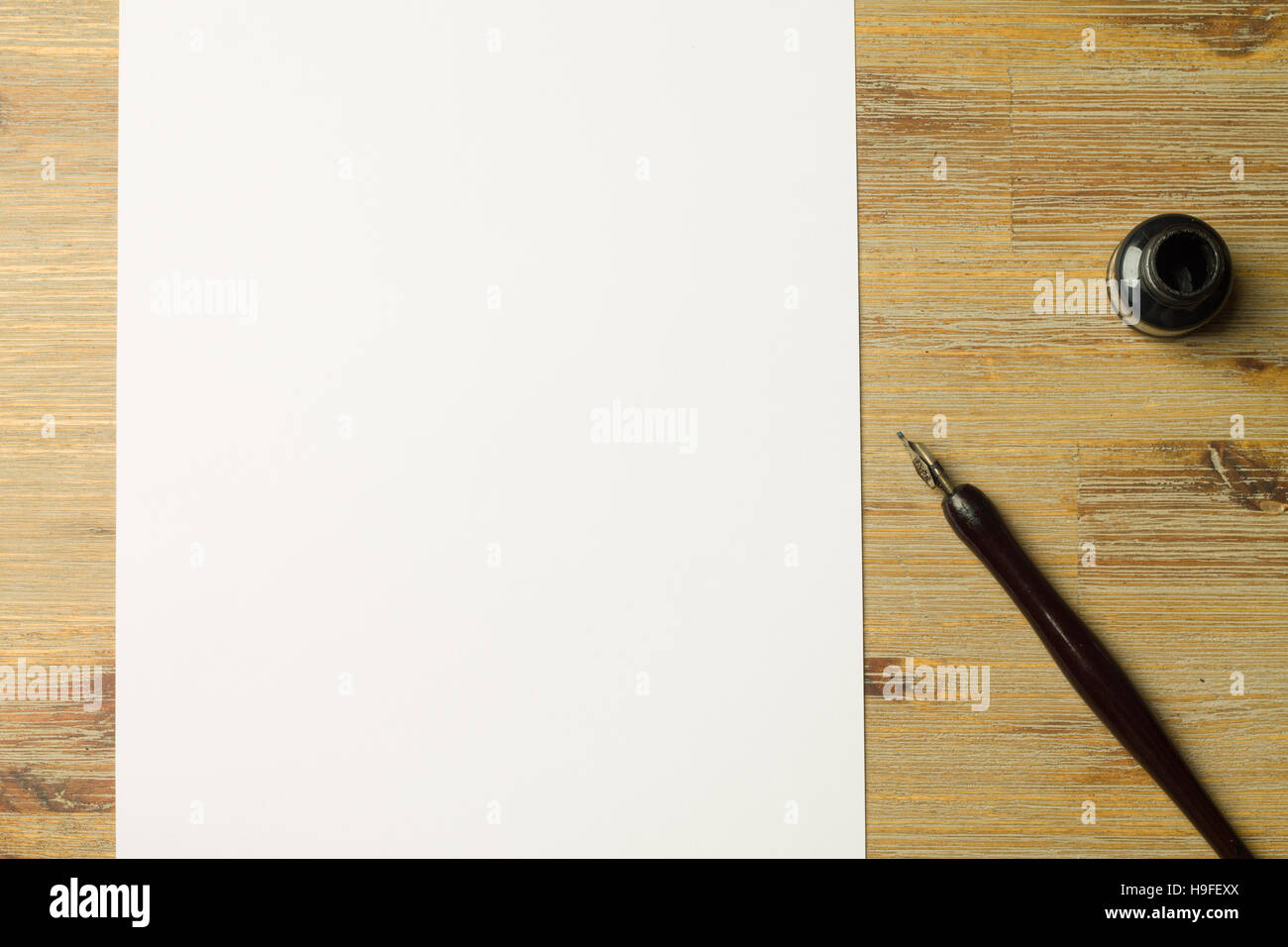 Fully visible blank sheet of paper, ink and pen on bright wooden office ...