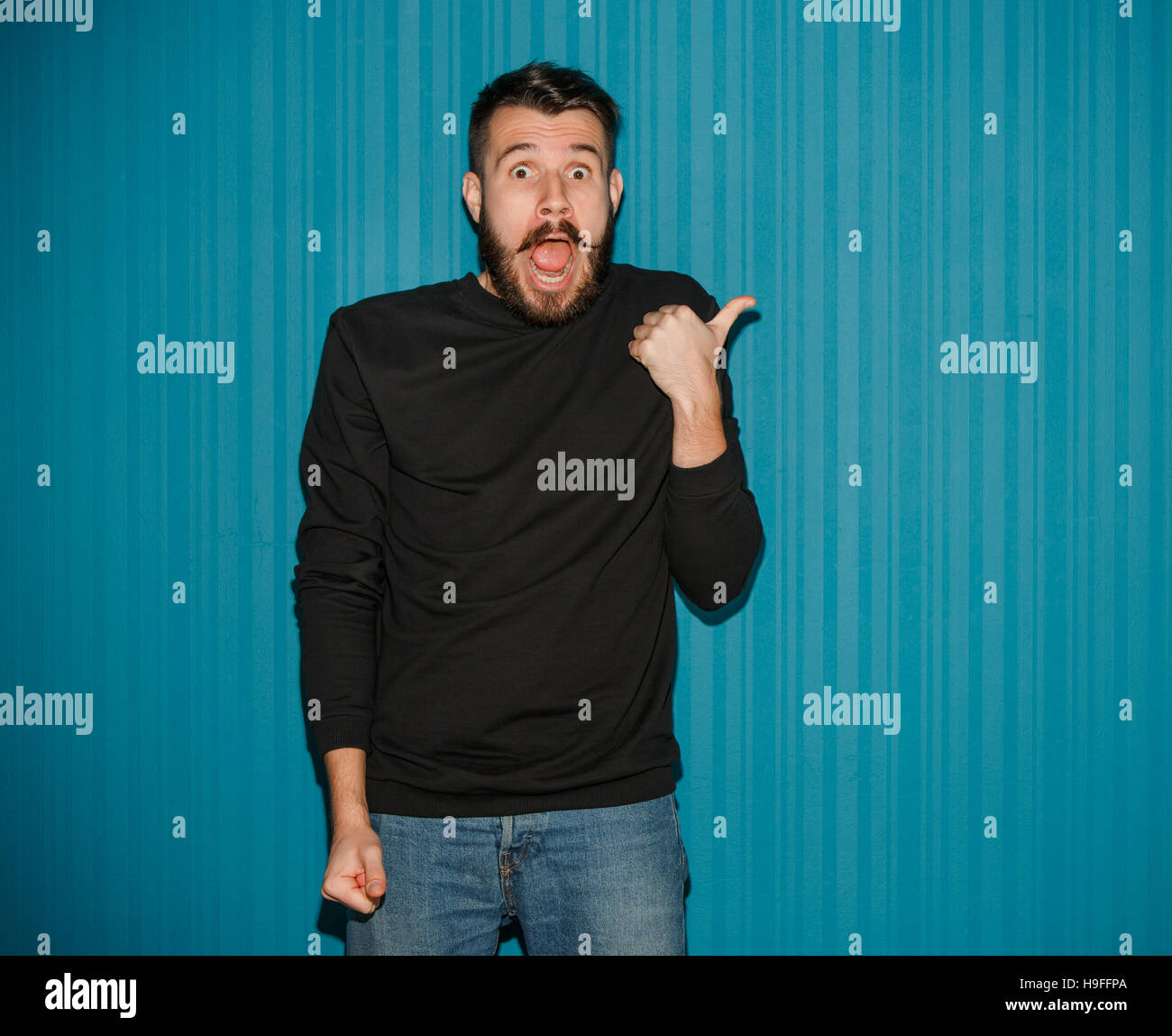 Portrait of young man with shocked facial expression pointing to the ...