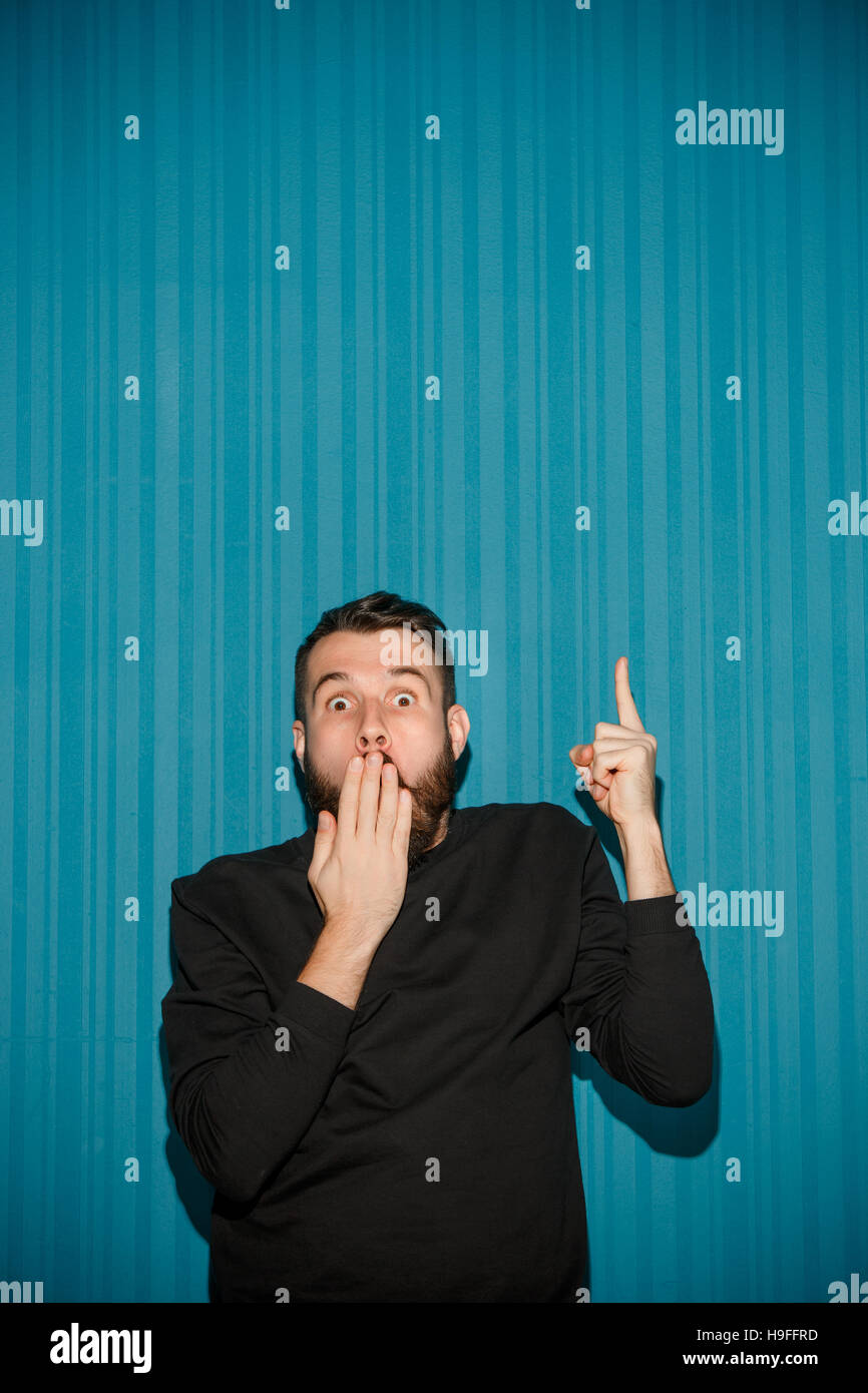 Portrait of young man with shocked facial expression pointing up over ...