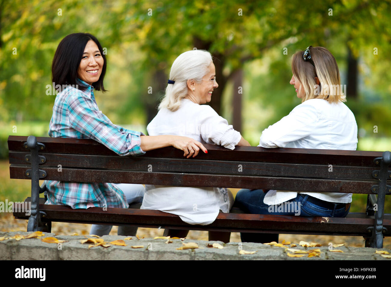 Three ladies sitting on the bench and having a conversation in the park ...