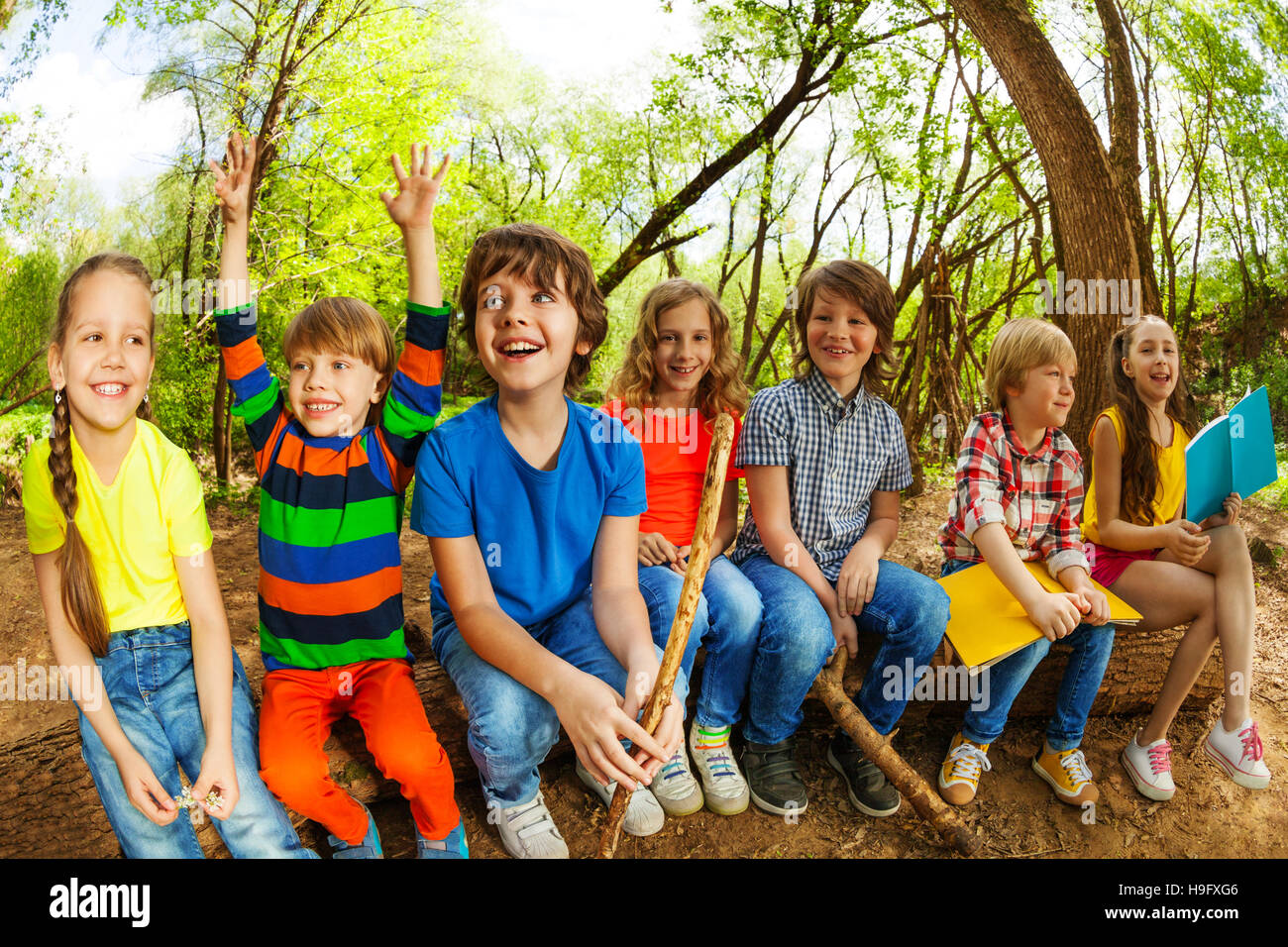 Happy kids sitting on a log and reading books Stock Photo - Alamy