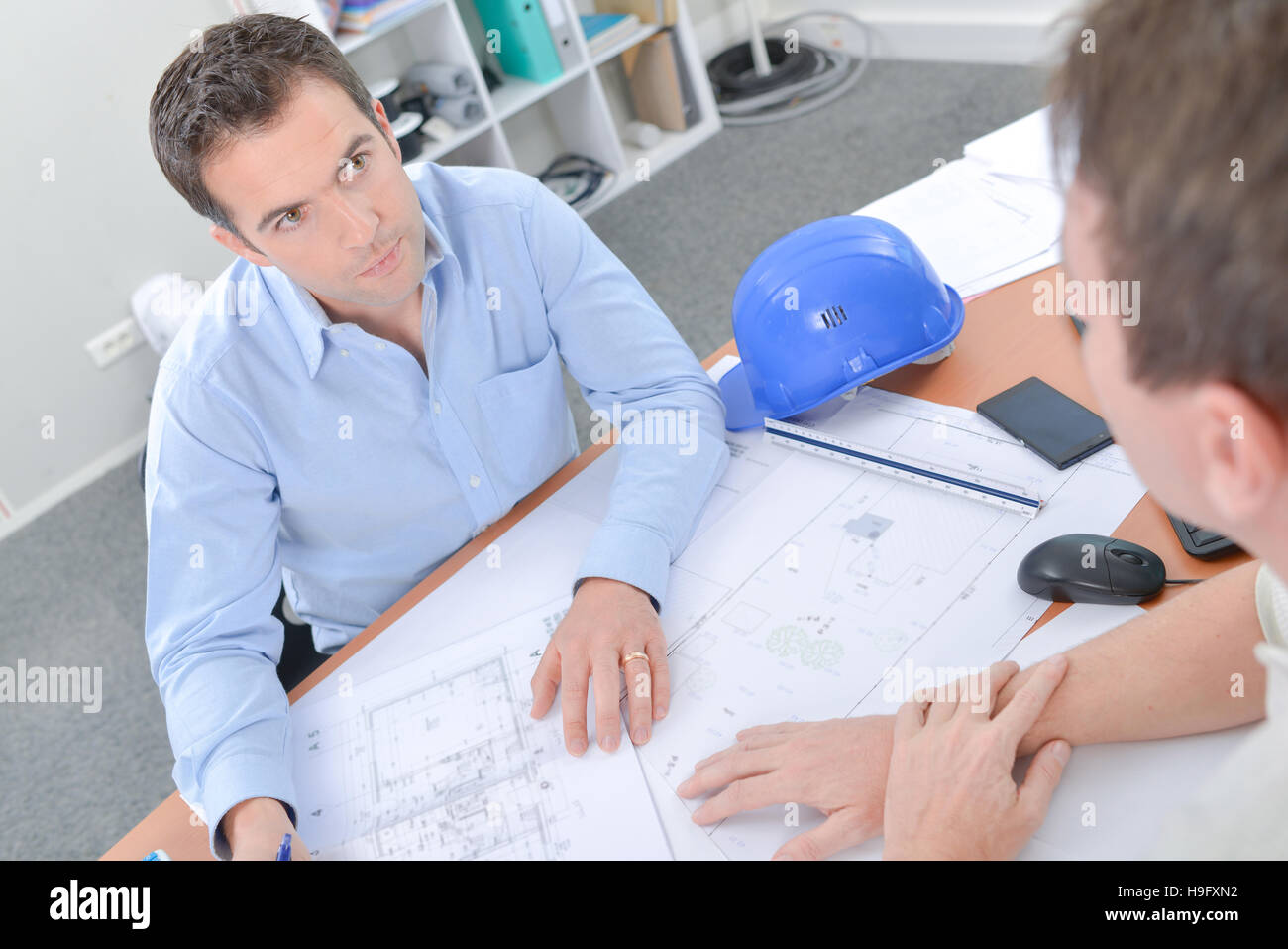 Two men at desk looking at blueprints Stock Photo - Alamy