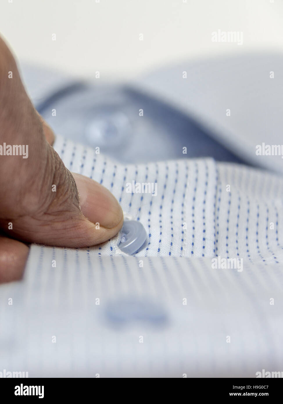 An image of a finger buttoning a blue shirt with dotted stripes Stock ...