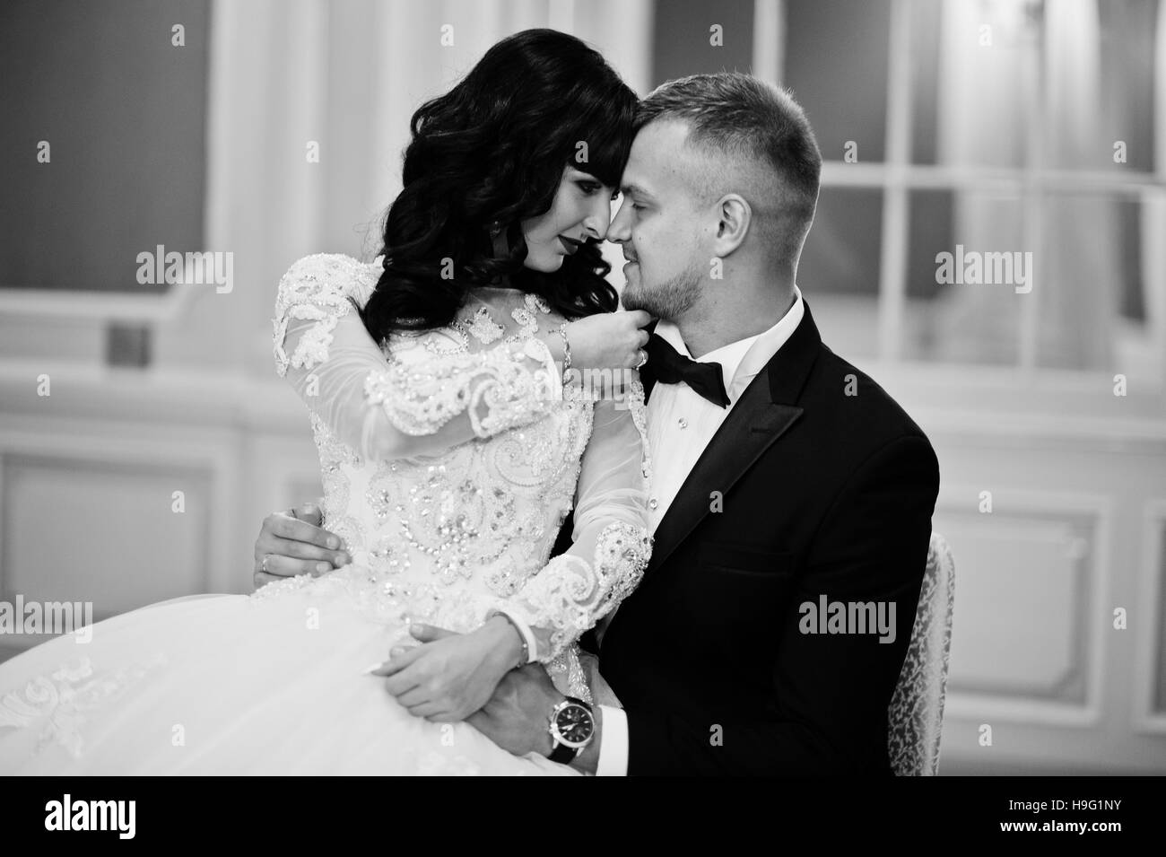 Magnificent wedding couple sitting on chair on royal room with many ...