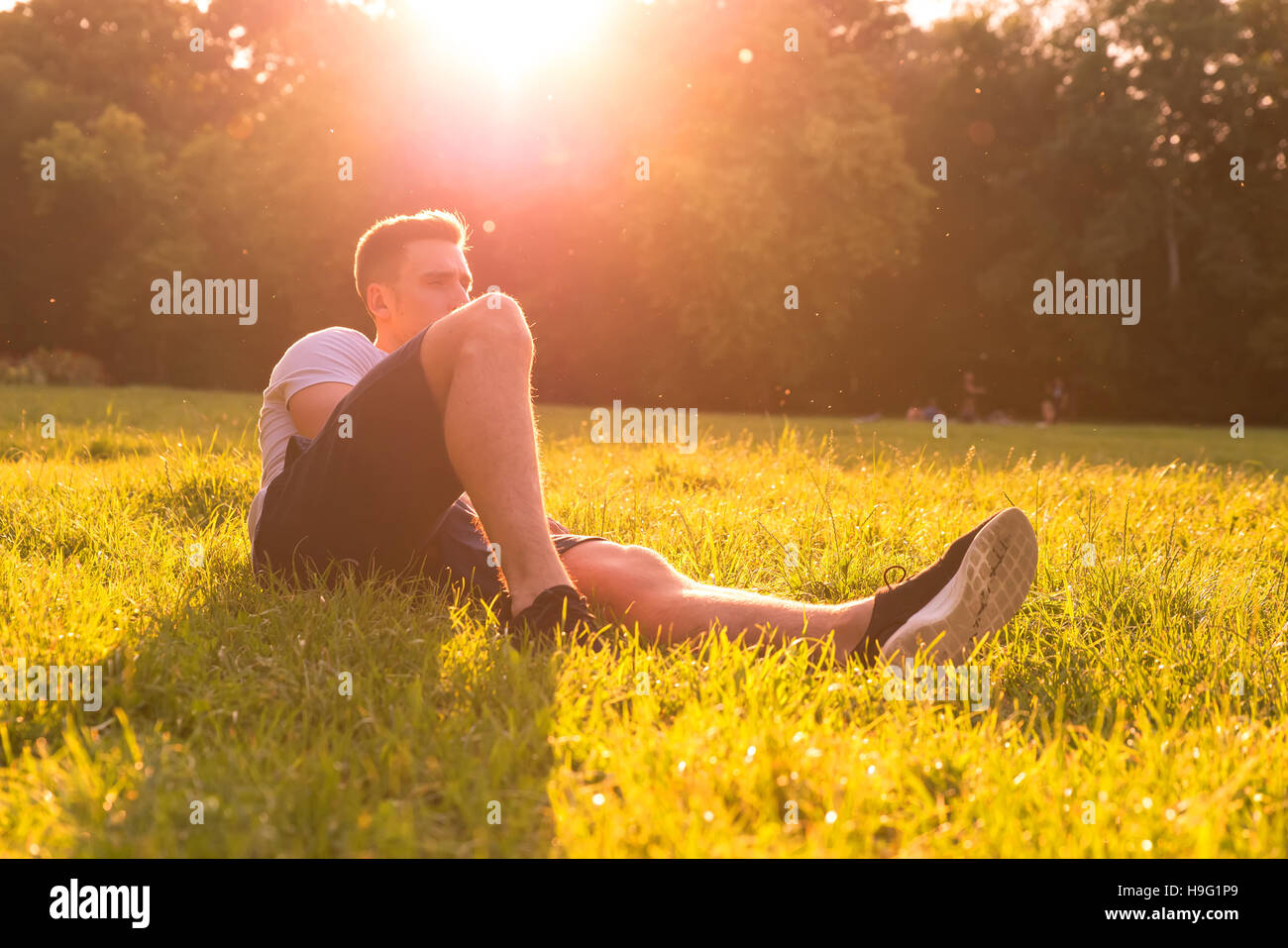 A handsome young man relaxing in the sunset and sitting in the grass ...