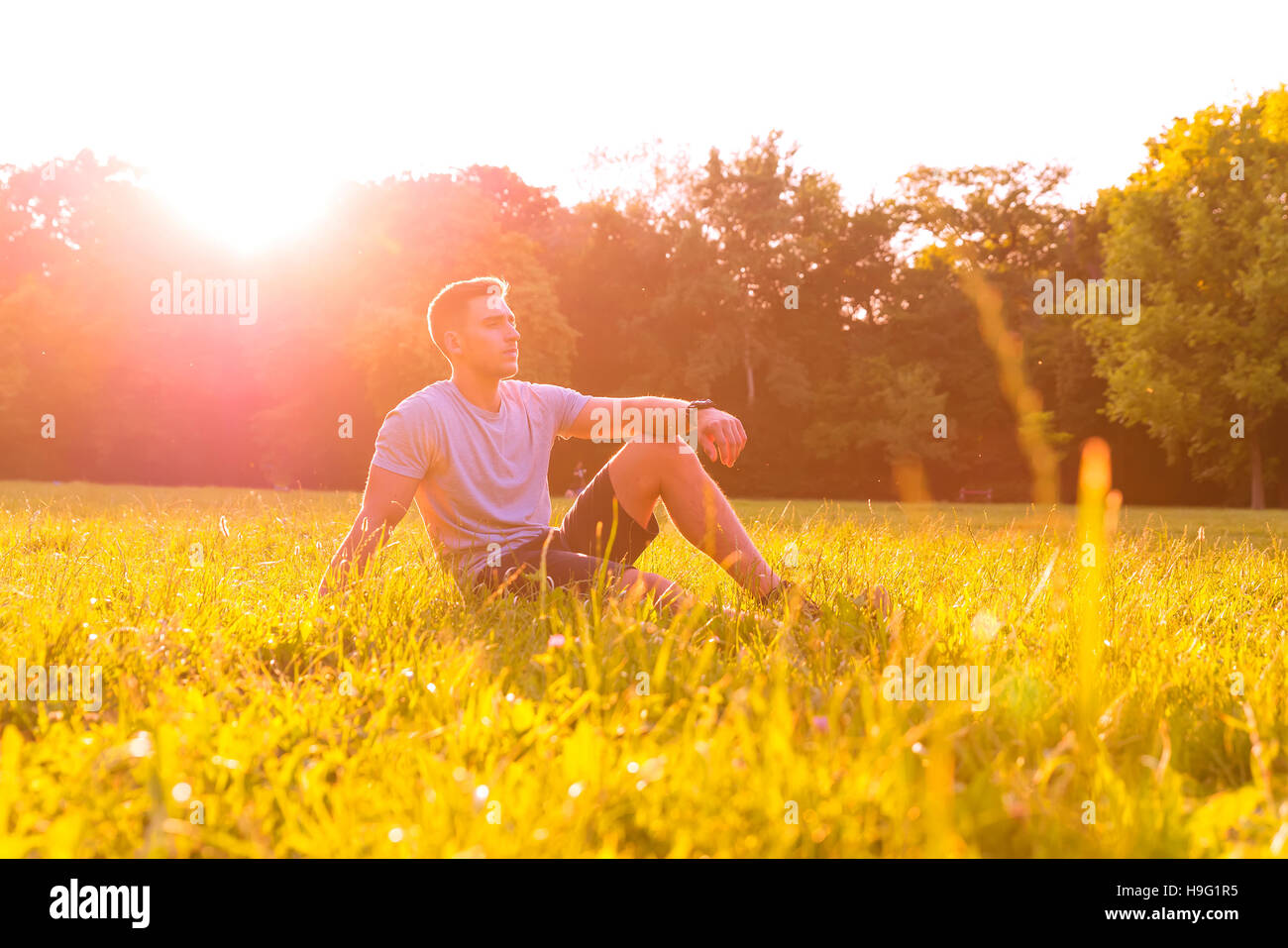 A handsome young man relaxing in the sunset and sitting in the grass ...