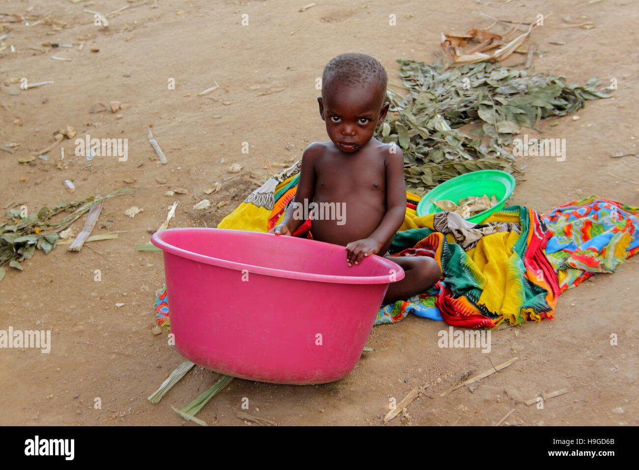 A small semi-naked child plays with a pink water bowl on a colorful ...