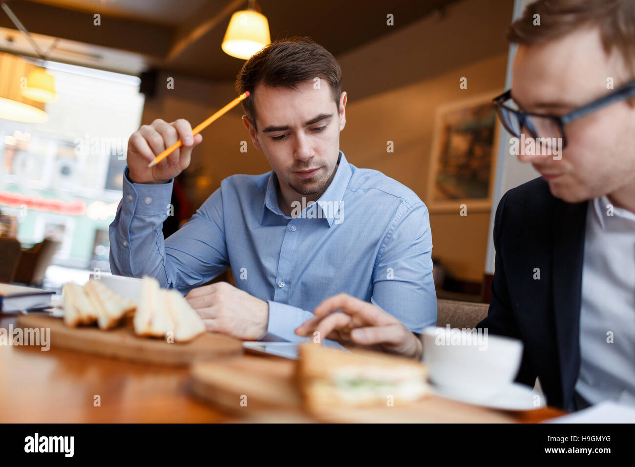 Pensive young man looking at touchpad screen during lunch break with co ...