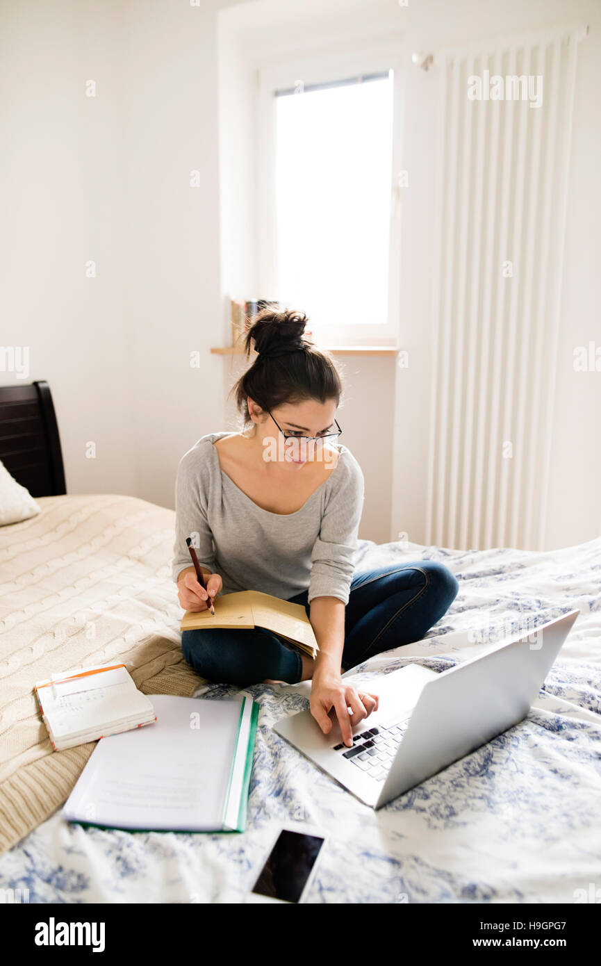Beautiful young woman sitting on bed, working. Home office Stock Photo ...