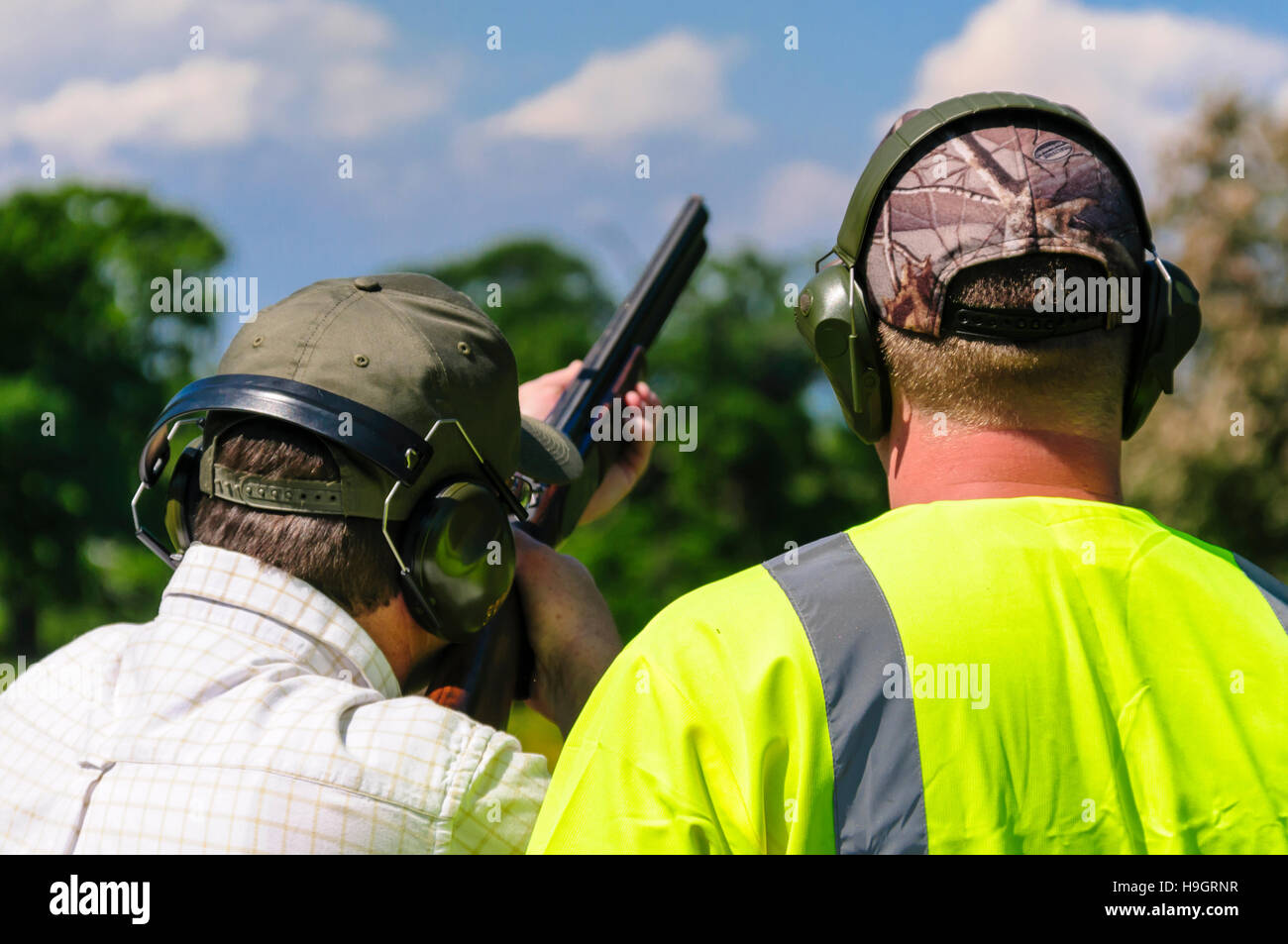 A man takes aim with a shotgun as an instructor watches closely Stock ...