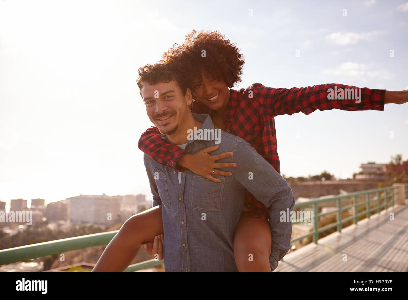 Playful young couple playing aeroplane her left arm out and holding ...