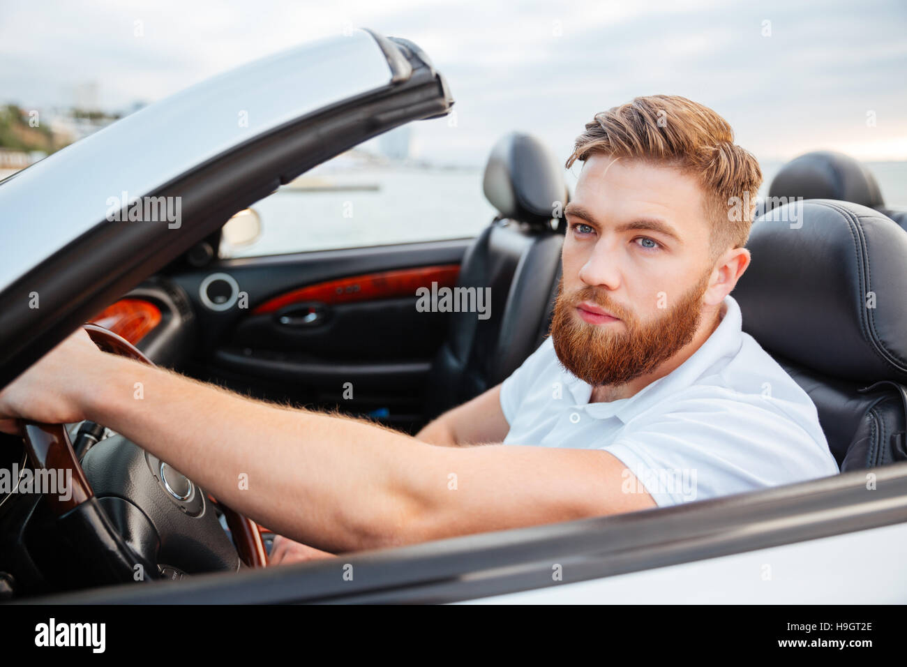 Handsome young man in white shirt driving his new car Stock Photo - Alamy