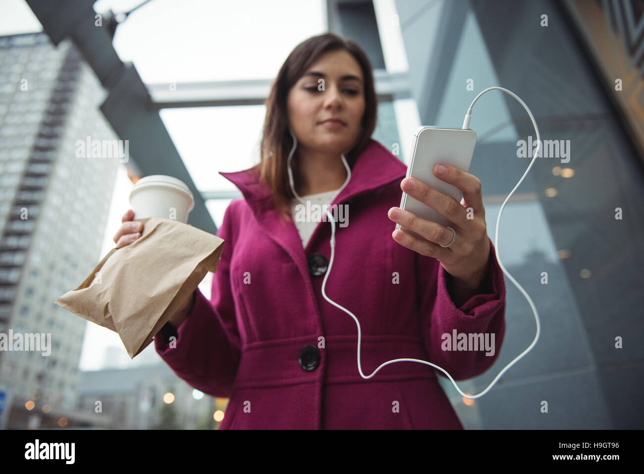 Businesswoman holding disposable coffee cup and parcel while listening ...