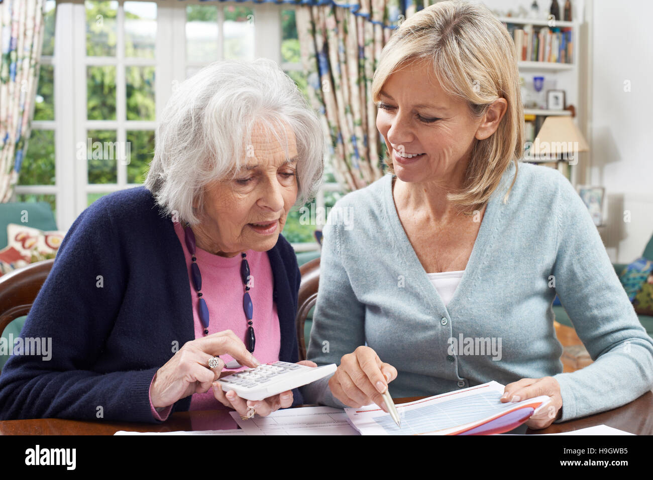 Female Neighbor Helping Senior Woman With Domestic Finances Stock Photo ...