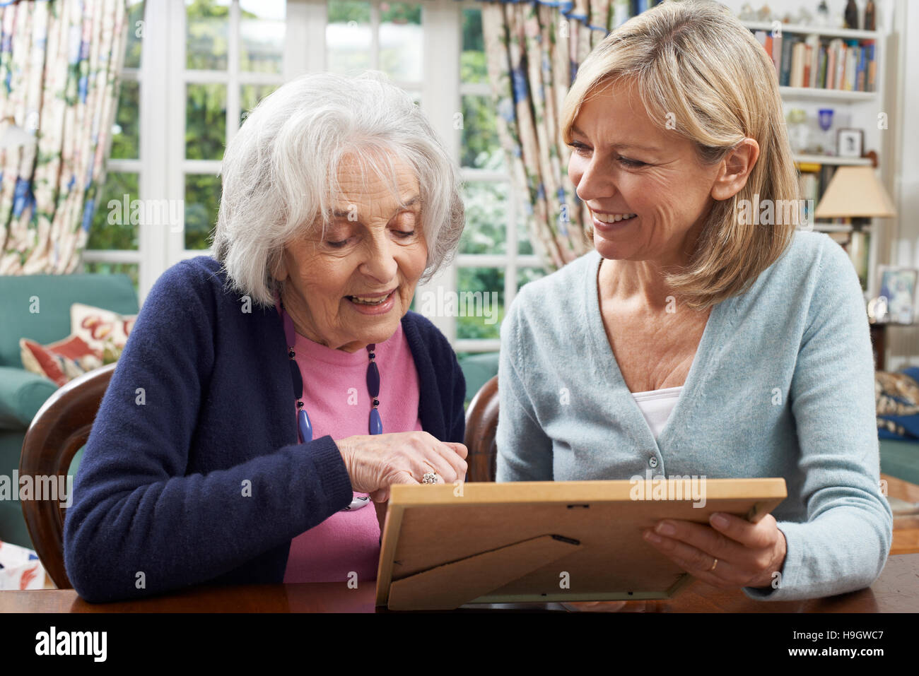Senior Woman Looks At Photo In Frame With Mature Female Neighbor Stock ...