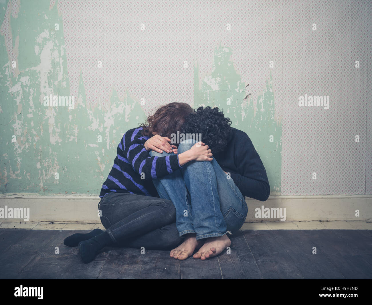 A sad young couple is sitting huddled up on the floor in an empty room ...