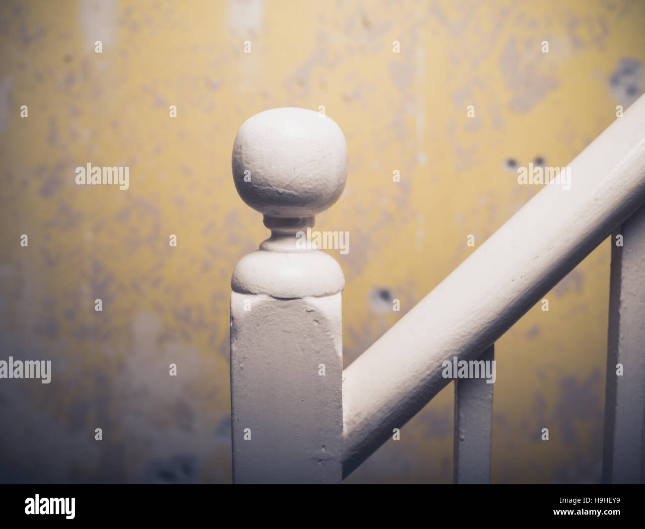 A banister and post in an old victorian house with a chipped wall in ...