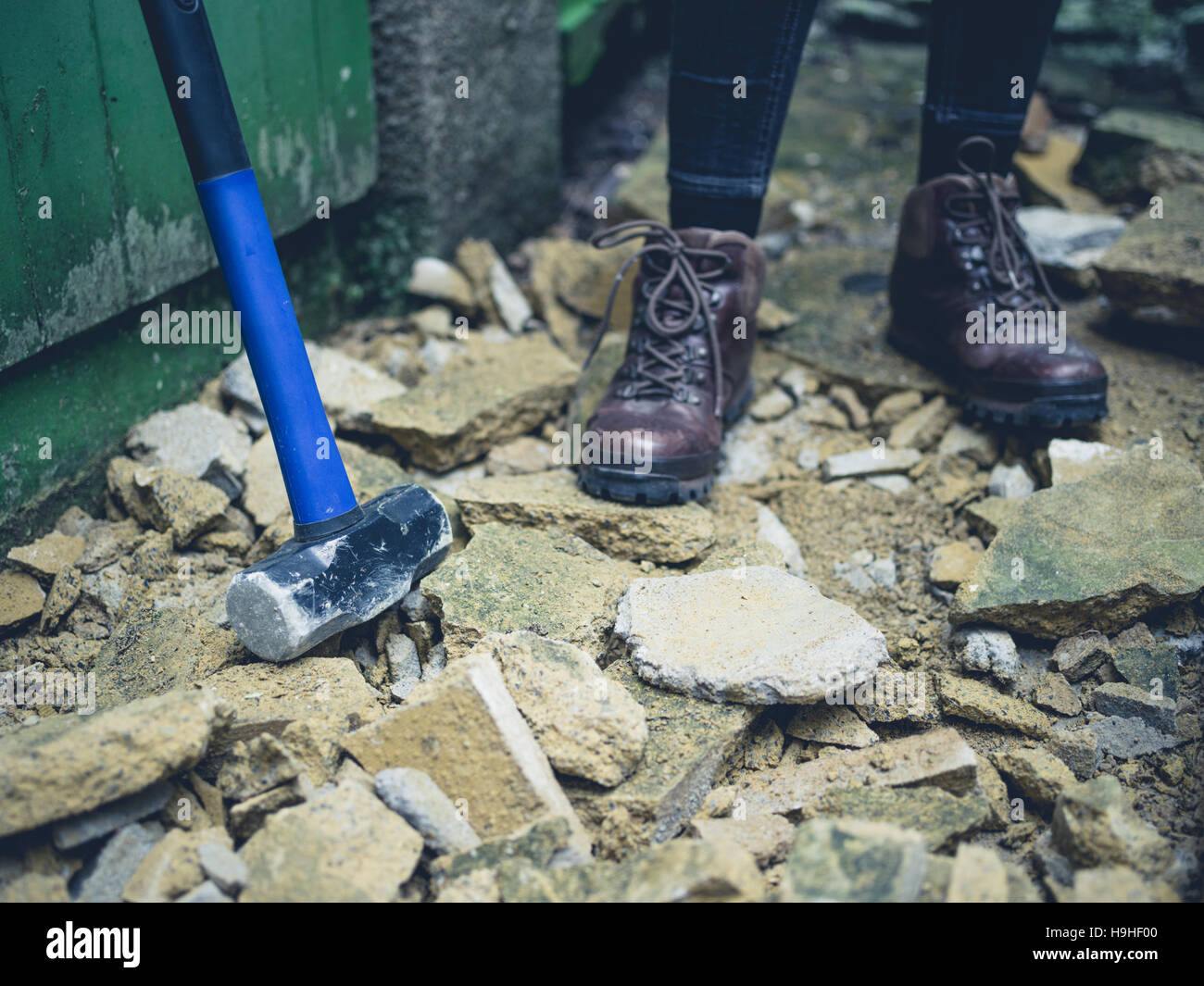 A person standing outside on rubble with a slege hammer by their feet ...