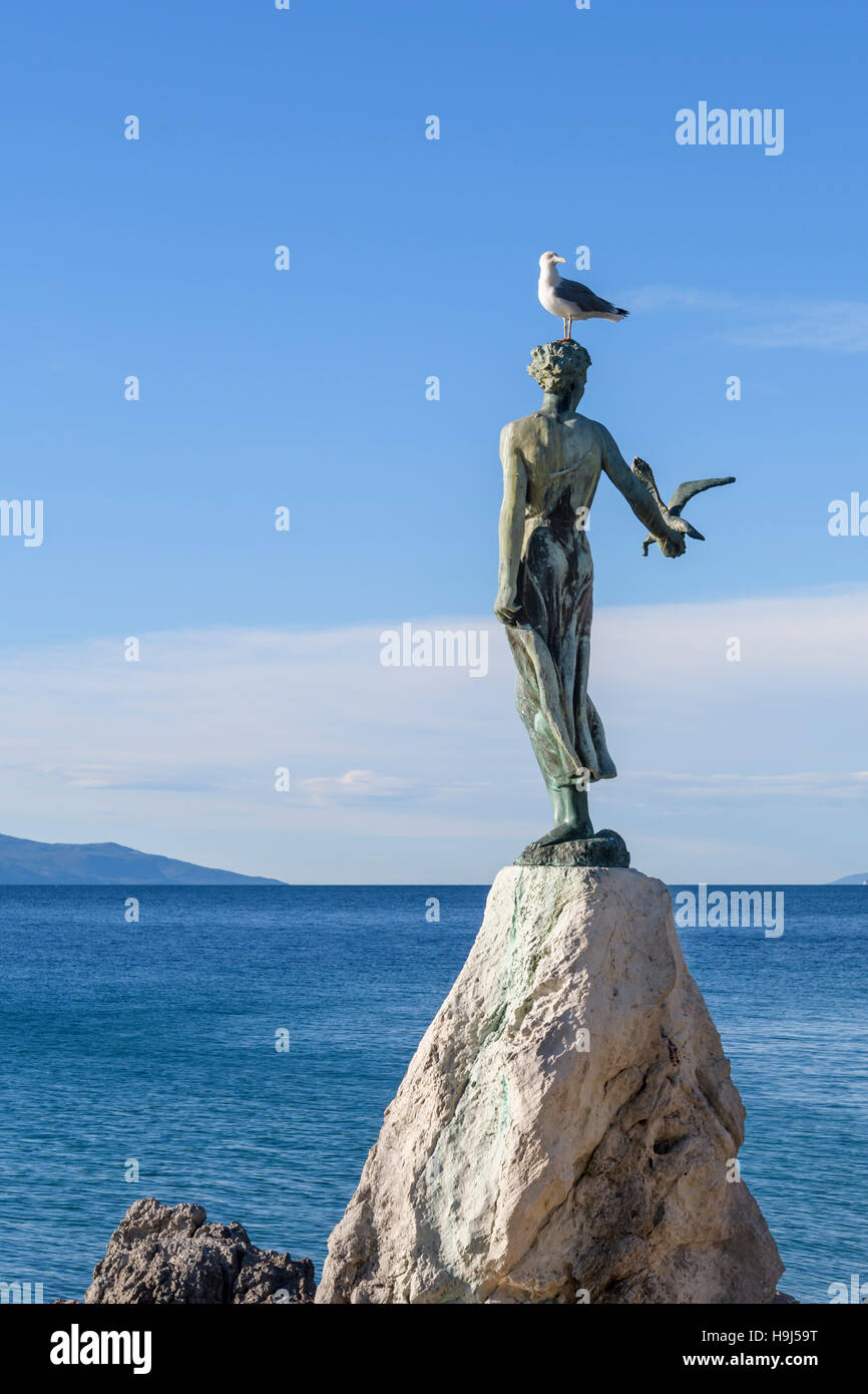 Maiden girl holding a seagull and facing the sea, statue on rocks ...