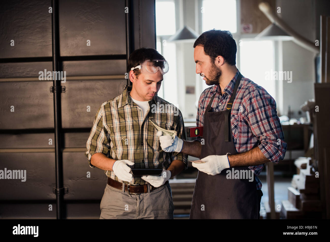 Two carpenters are talking while holding papers and ruler. One of them ...