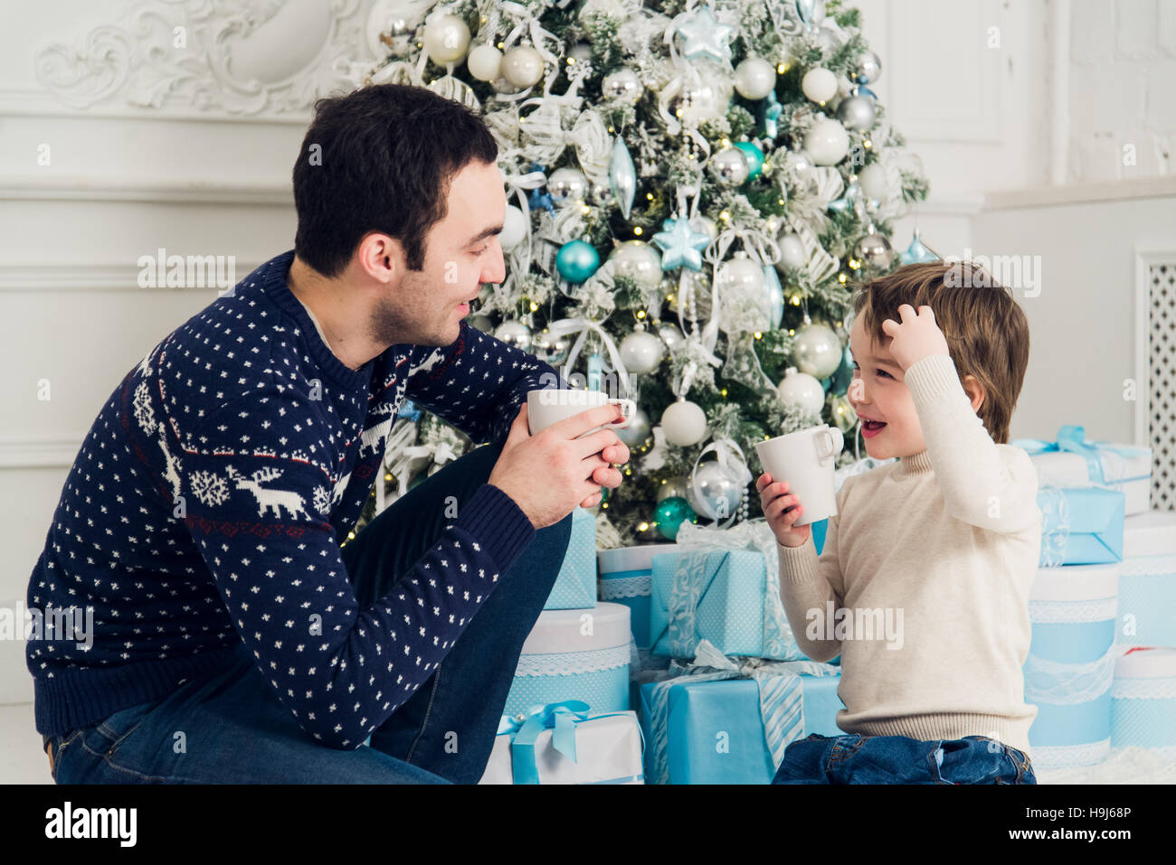 Happy dad and son with cups of tea talking near Christmas time at home ...