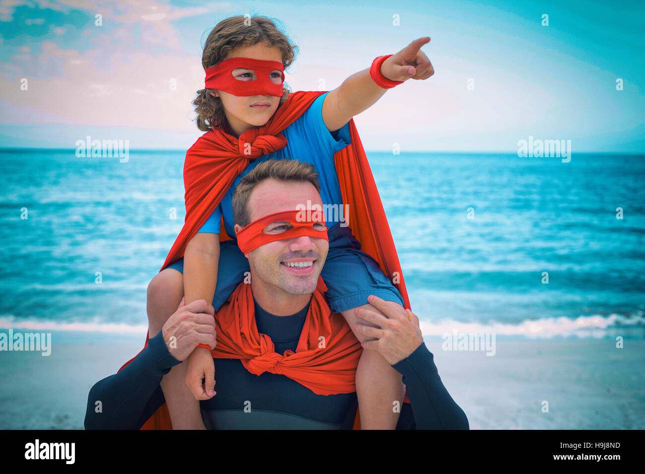 Son in superhero costume pointing while father carrying on shoulder ...