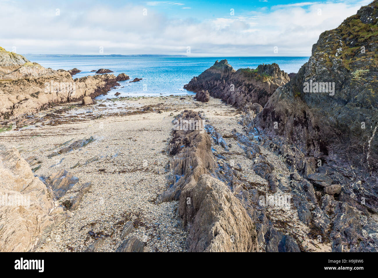 Looking out to sea across a small sandy cove lined with rocky outcrops ...