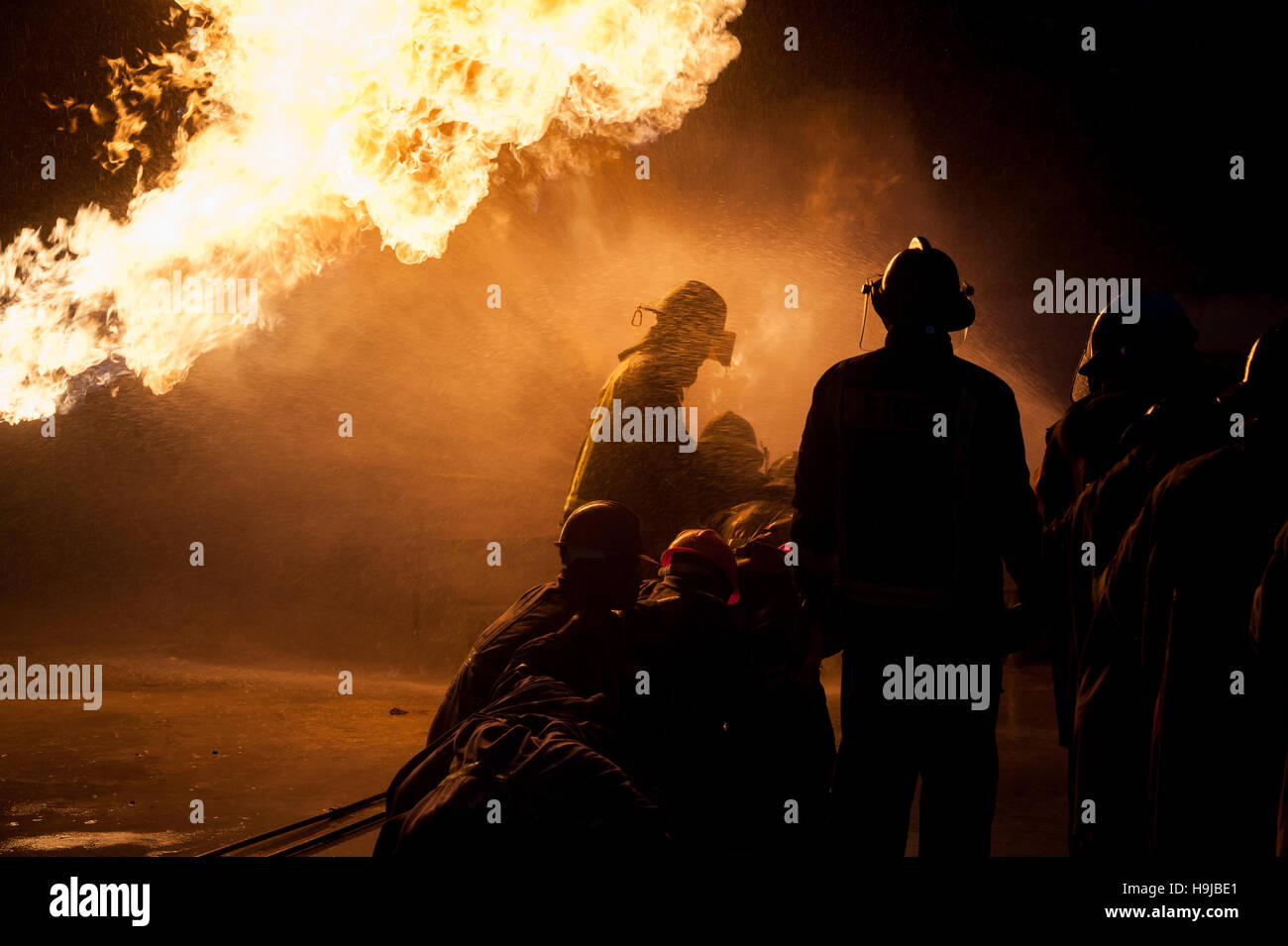 Silhouette of Firemen fighting a raging fire with huge flames of ...