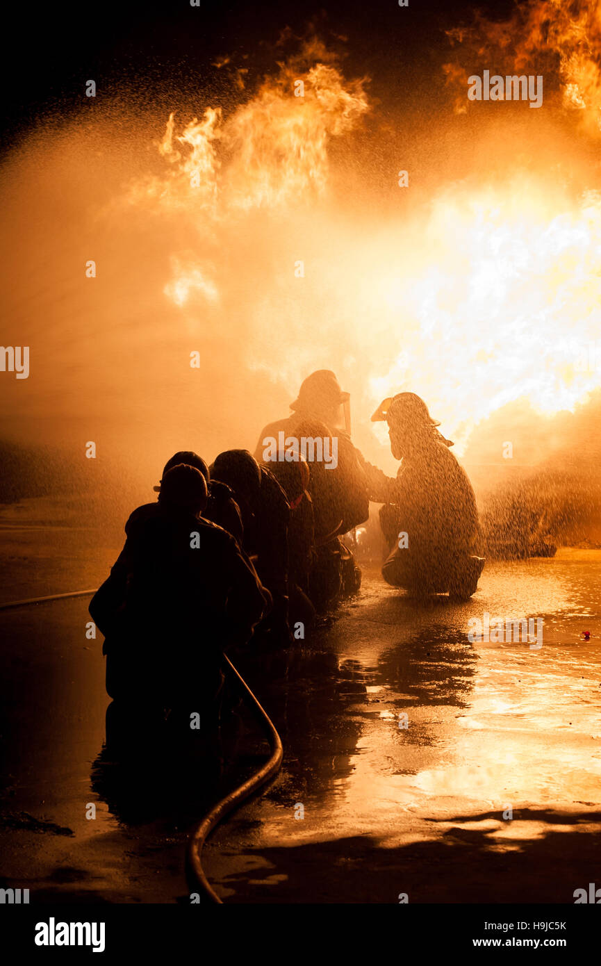 Silhouette of Firemen fighting a raging fire with huge flames of ...