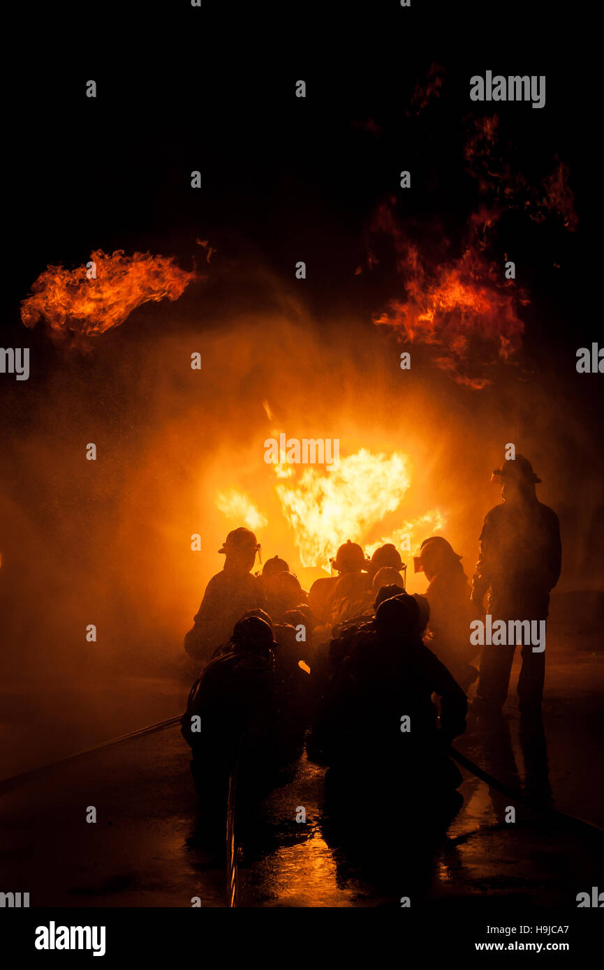 Silhouette of Firemen fighting a raging fire with huge flames of ...