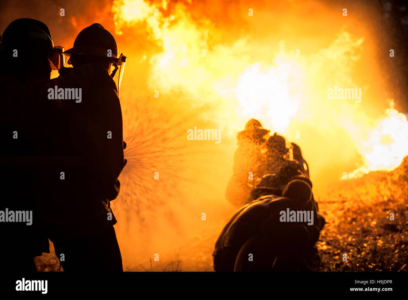 Silhouette of Firemen fighting a raging fire with huge flames of ...